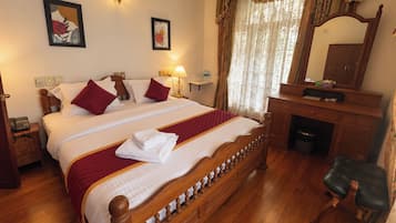 Quarto de hotel com uma cama grande, cabeceira de madeira, uma escrivaninha com espelho e uma cadeira.