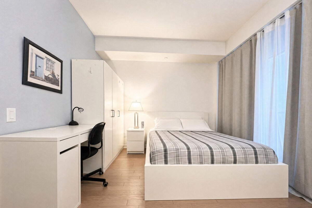 Quarto com cama, escrivaninha, cadeira, mesa de cabeceira, abajur e janela com cortinas.