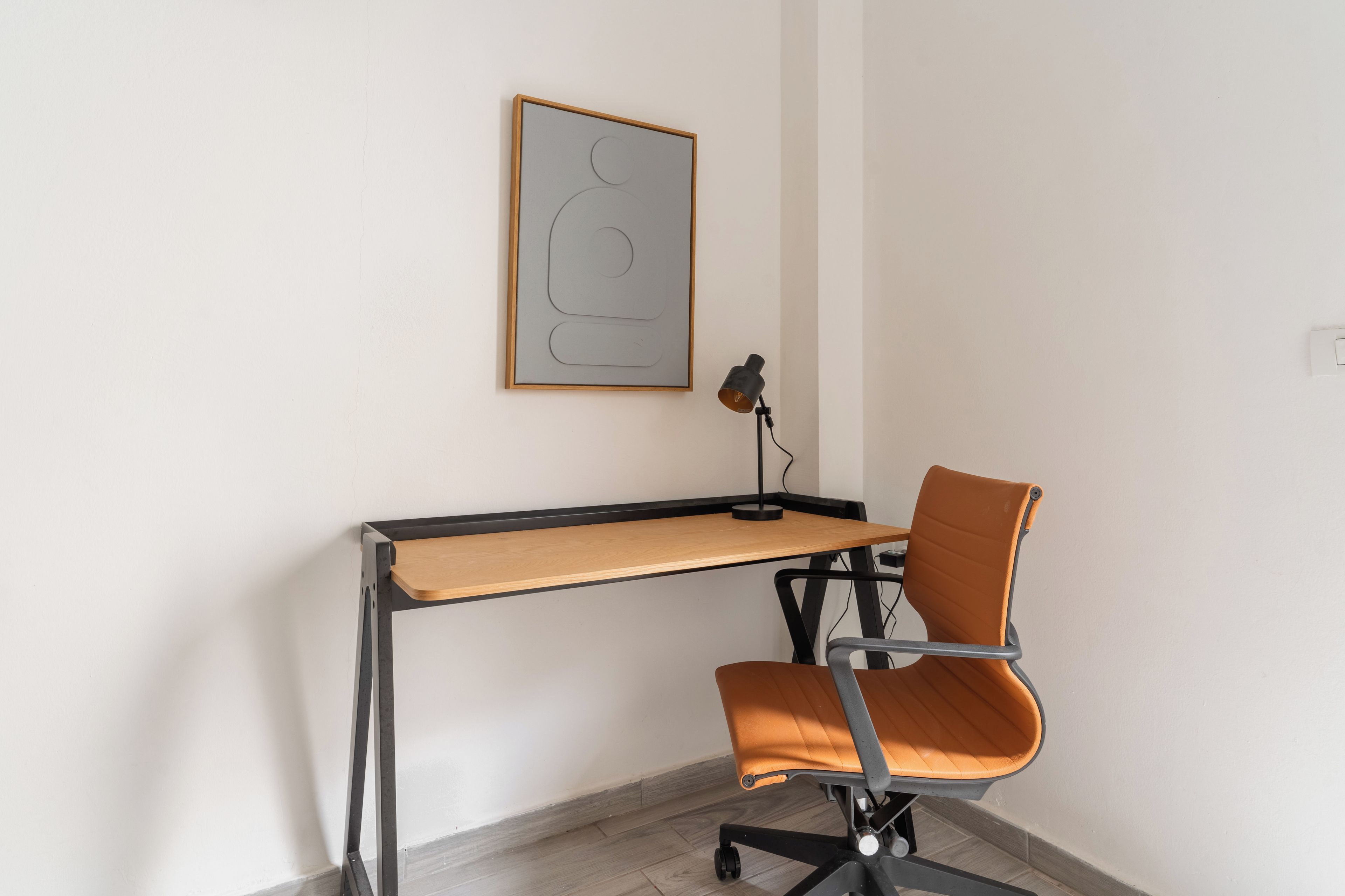 Um espaço de trabalho com escrivaninha, cadeira e uma obra de arte abstrata emoldurada na parede.