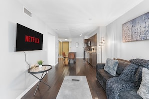 Uma sala de estar moderna com televisão de tela plana, um sofá, uma mesa de centro e uma área de jantar ao fundo.