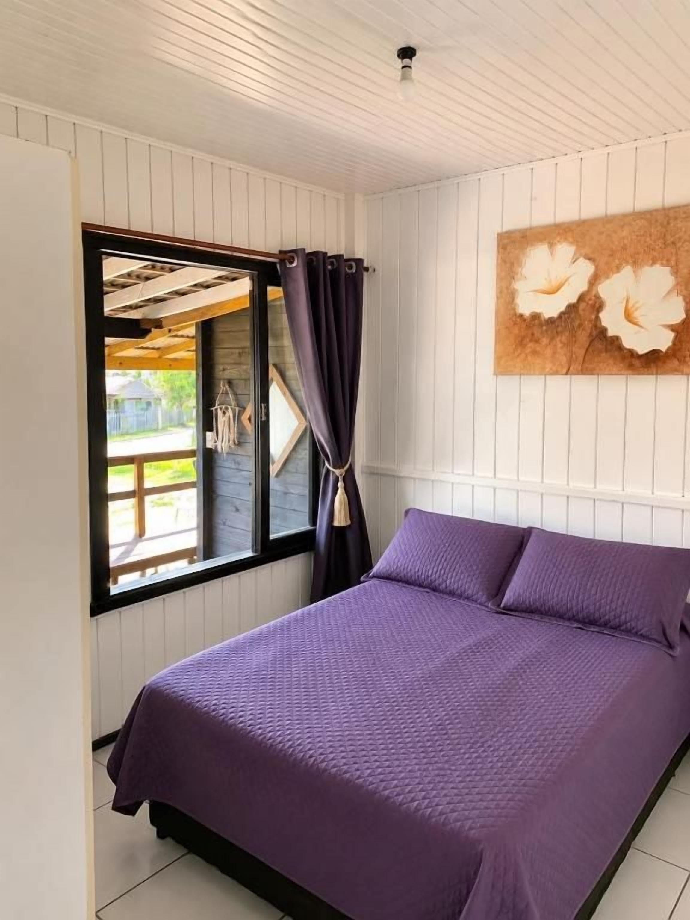 Quarto com cama, janela com cortinas e uma obra de arte pendurada na parede.