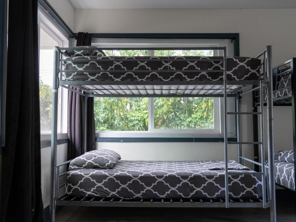 Uma cama beliche com roupa de cama estampada, uma janela com cortinas e vista para o verde lá fora.