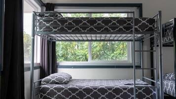 Uma cama beliche com roupa de cama estampada, uma janela com cortinas e vista para o verde lá fora.