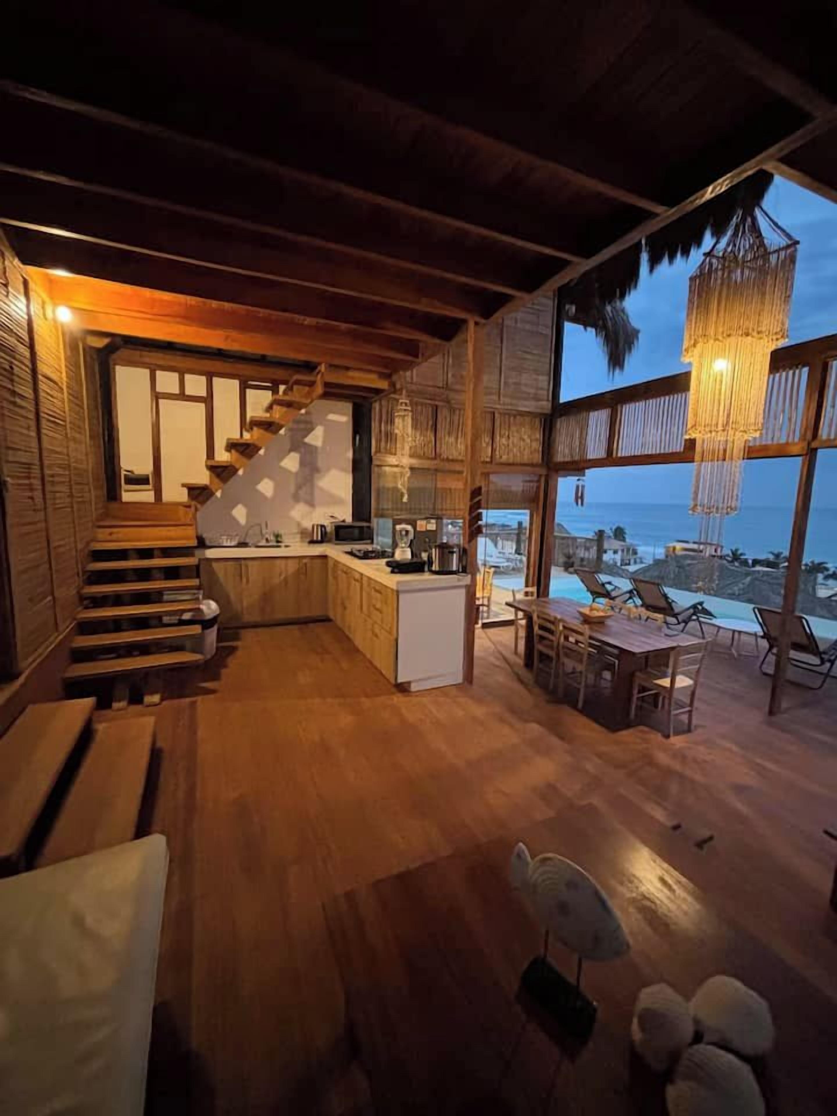Cozinha espaçosa com vista para o oceano, piso de madeira e área de refeições com assentos externos.