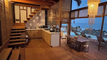 Cozinha espaçosa com vista para o oceano, piso de madeira e área de refeições com assentos externos.