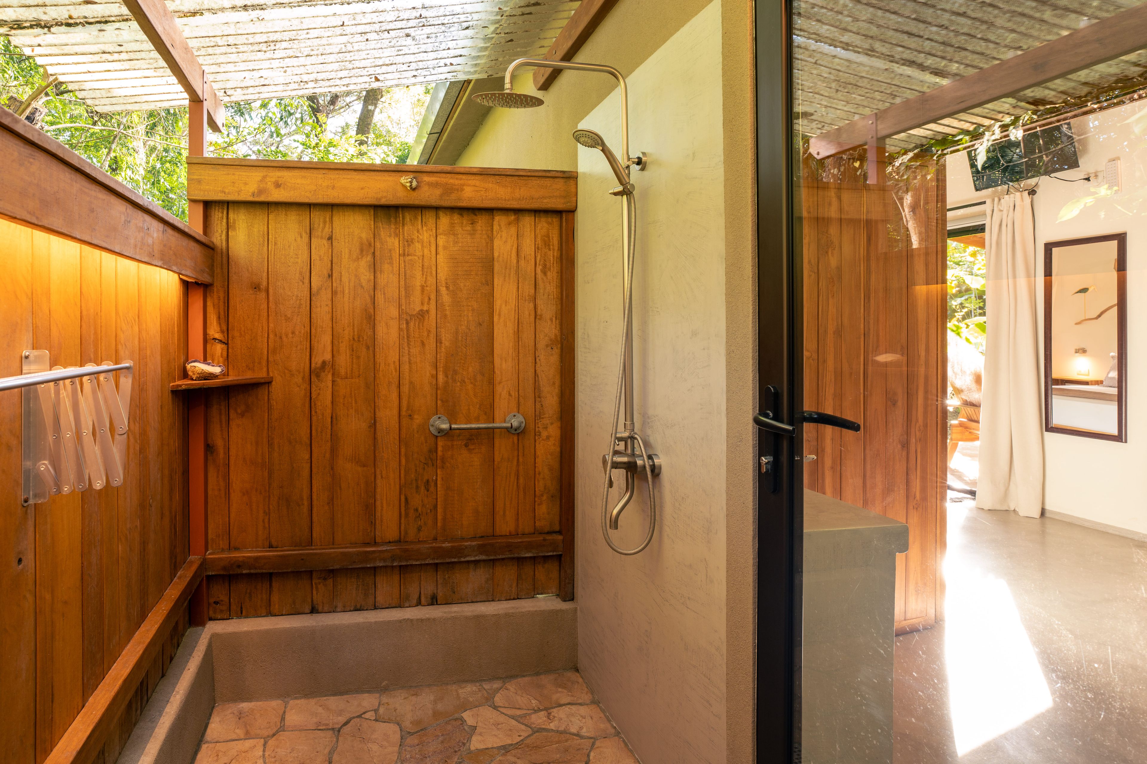 Porta de madeira que dá para um espaço com chuveiro, um chuveiro de metal e um porta-toalhas.