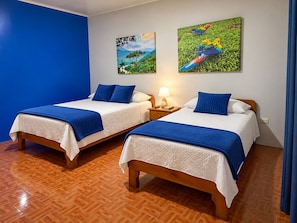 Quarto de hotel com duas camas, uma mesa de cabeceira com abajur e duas pinturas penduradas na parede.