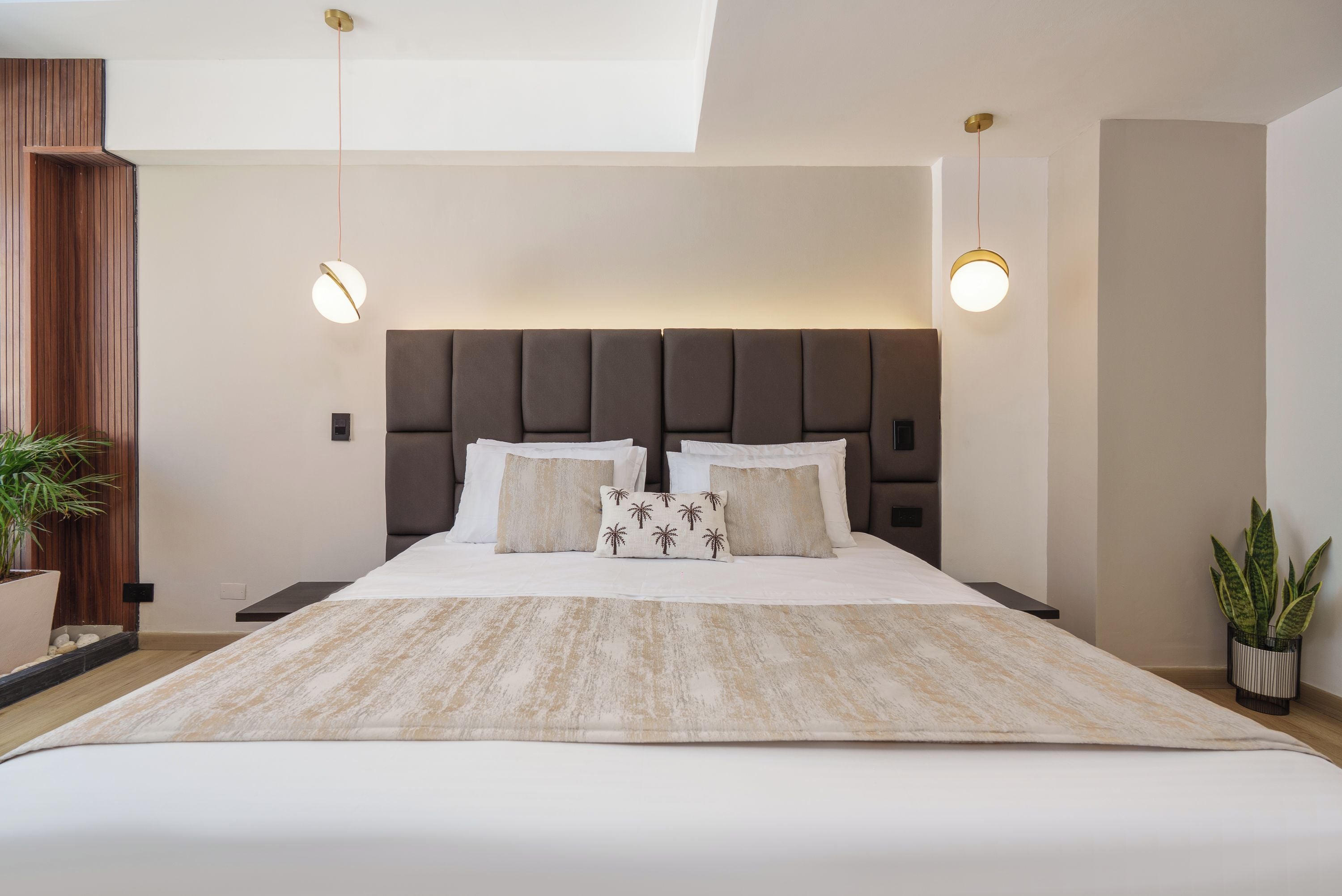 Quarto moderno com uma cama grande, cabeceira, abajures e um vaso com planta.