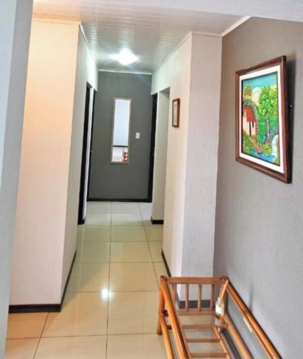 Um corredor com um banco de madeira, um quadro pendurado na parede e uma porta no final.
