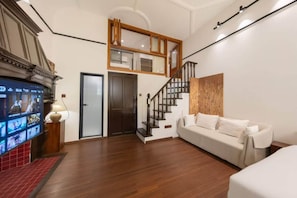 Uma sala de estar ampla com escada de madeira, televisão de tela plana e sofá branco.