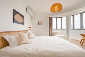 Quarto moderno com cama grande, vista para a cidade e luminária pendente original.