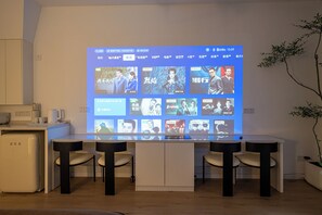 Tela de projeção exibindo uma seleção de filmes e séries em um ambiente moderno com design minimalista, com uma mesa e cadeiras.