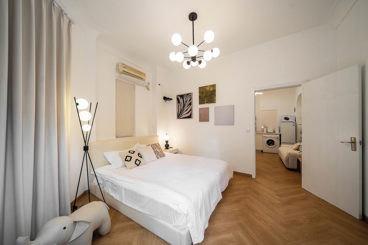 Quarto com cama, abajures, ar condicionado fixado na parede e corredor que dá para um banheiro.
