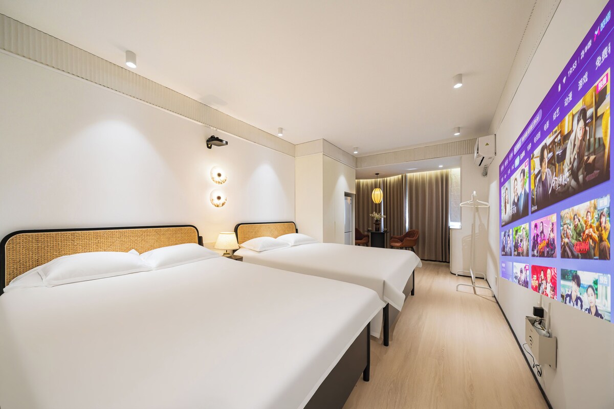 Quarto de hotel com duas camas, televisão na parede e área de estar com mesa e cadeiras.
