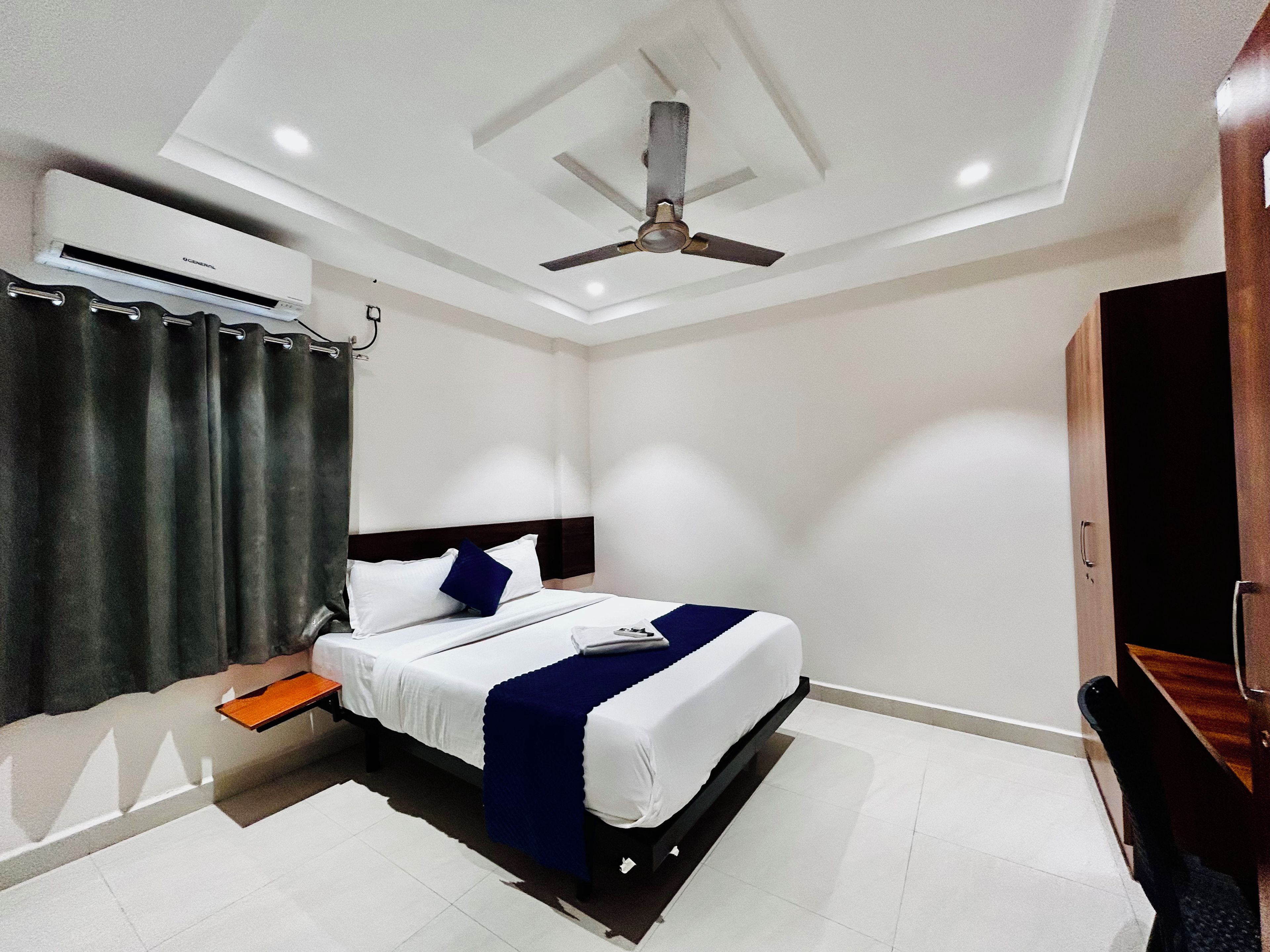 Quarto de hotel com cama, ventoinha no teto, ar condicionado e guarda-roupa de madeira.