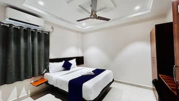 Quarto de hotel com cama, ventoinha no teto, ar condicionado e guarda-roupa de madeira.