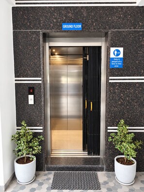 Entrada de elevador com placa indicando 'PISO TERREO' e aviso informando 'Apenas 4 pessoas por vez nesta área'.