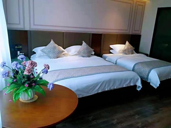 Quarto de hotel com duas camas, uma mesa redonda de madeira e um vaso de flores, além de uma grande janela.