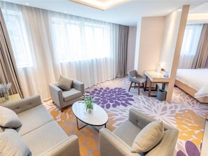 Quarto de hotel com uma cama, duas poltronas, uma escrivaninha e uma mesa de centro.