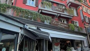 Um edifício vermelho com restaurante no andar térreo, placa com 'Hotel La Rouvière' e varanda com plantas.