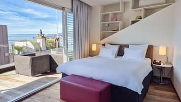 Quarto de hotel moderno com uma cama grande, um banco vermelho, varanda com vista e estantes embutidas.