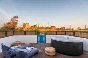 Terraço no telhado com banheira de hidromassagem, área de estar e vista para um castelo histórico.