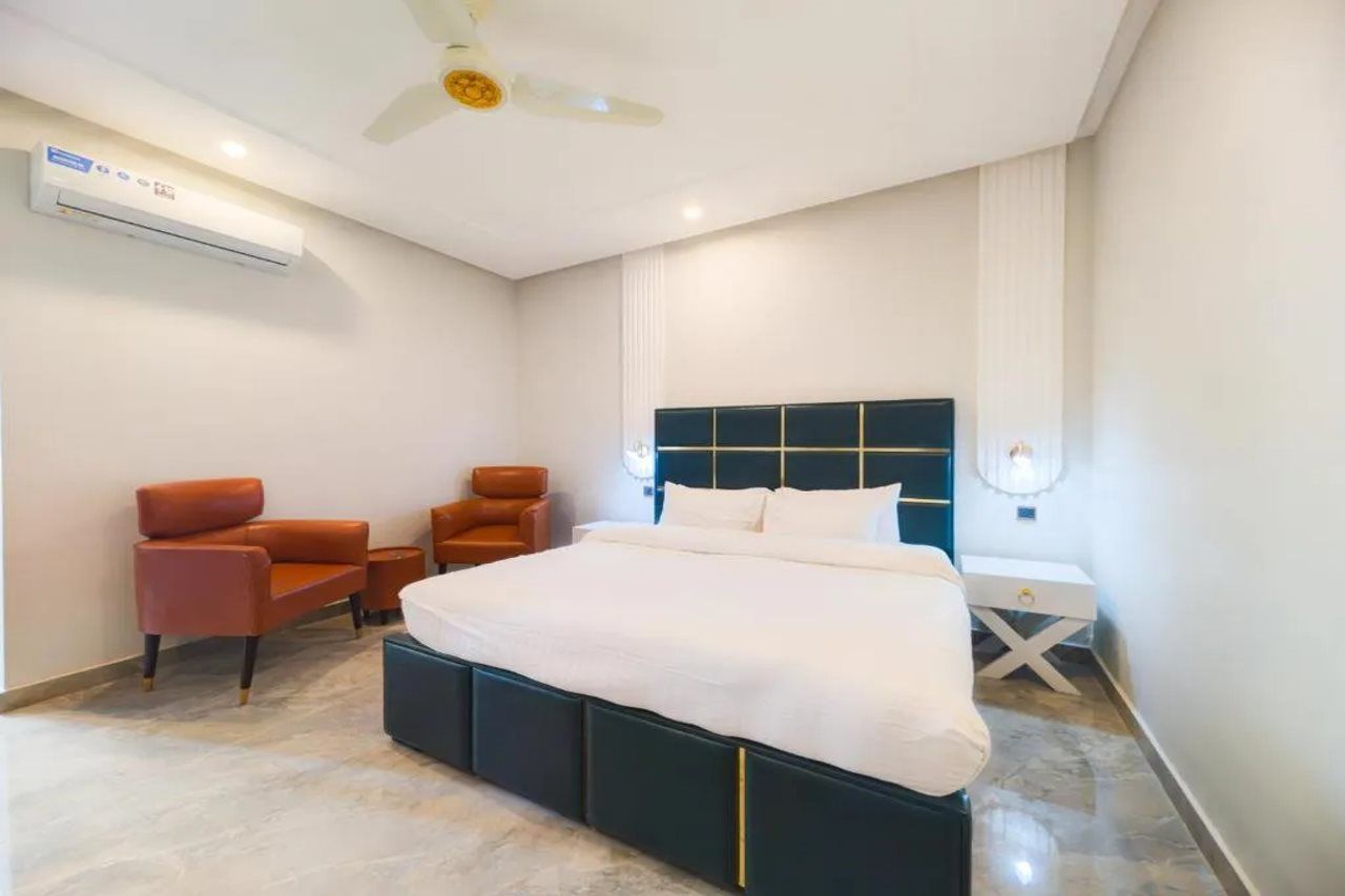 Quarto de hotel moderno com uma cama grande, duas poltronas, uma mesinha de cabeceira e um ventilador de teto.