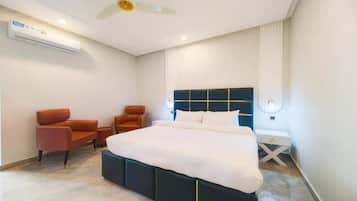 Quarto de hotel moderno com uma cama grande, duas poltronas, uma mesinha de cabeceira e um ventilador de teto.