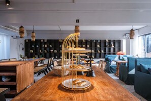 Interior moderno com mesa de jantar de madeira, suporte de sobremesas em três níveis e estante ao fundo.