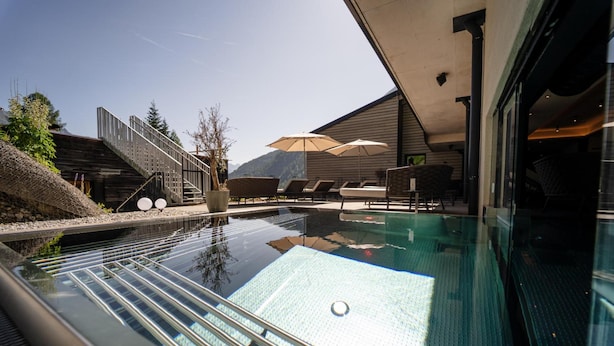 Piscina infinita com vista desimpedida das montanhas, cadeiras de descanso e um deck de madeira.