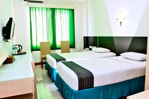 Quarto de hotel com duas camas, uma escrivaninha, uma cadeira, televisão e janela com cortinas.
