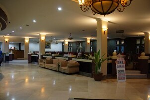 Um saguão de hotel com balcão de recepção, sofás e um candelabro.