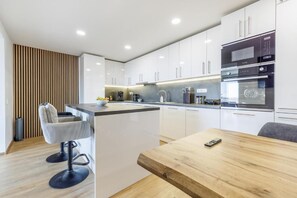 Cozinha moderna com armários brancos, mesa de jantar de madeira e um balcão com banquetas.
