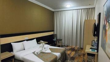 Quarto de hotel com cama, escrivaninha, cadeira, televisão e um quadro na parede.