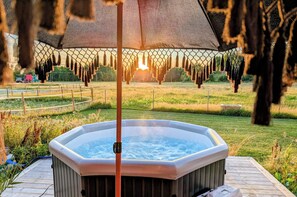 Uma banheira de hidromassagem em um jardim com um deck de madeira, cercada por grama e um muro.