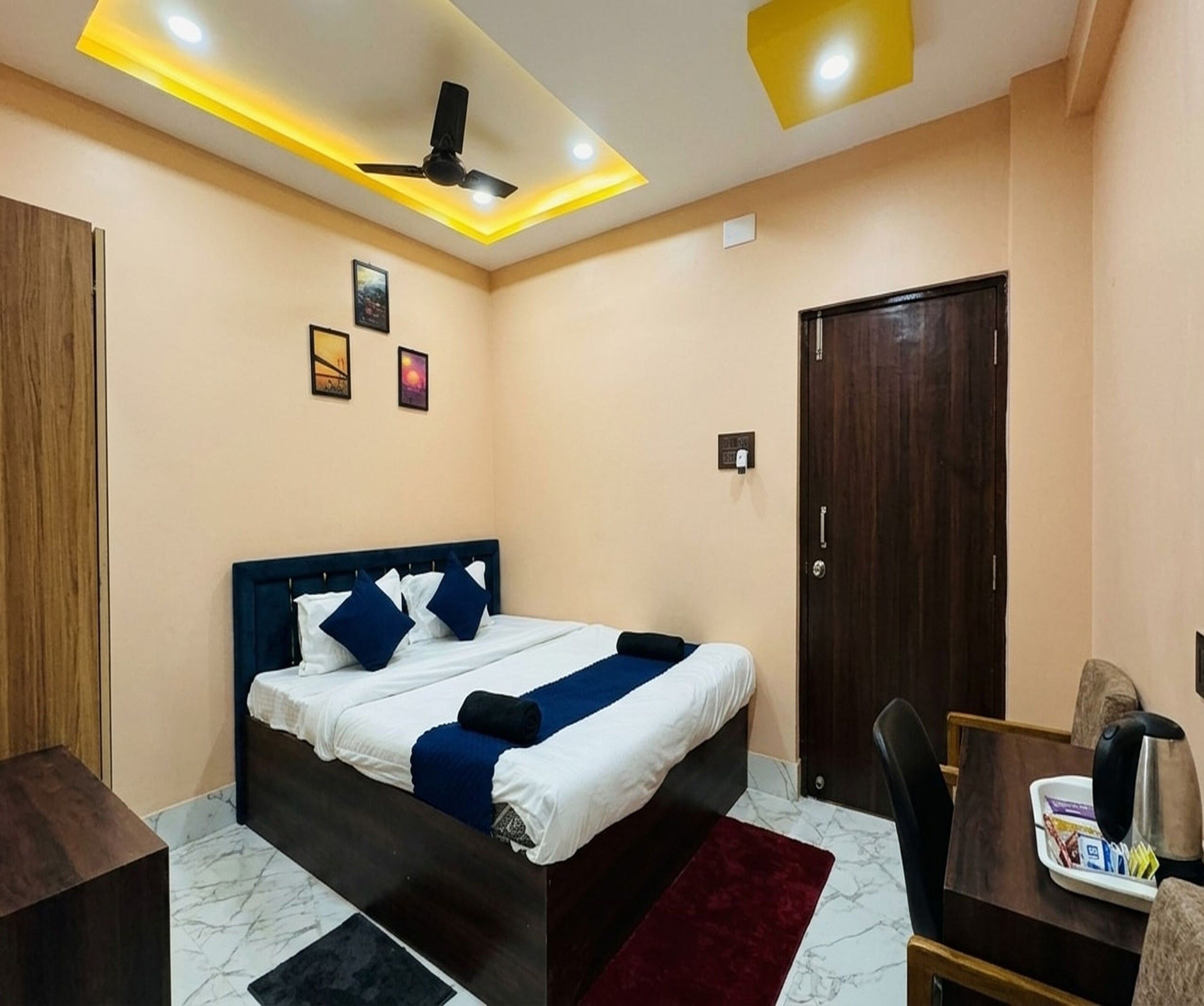 Quarto de hotel com cama, escrivaninha, cadeira, guarda-roupa e ventoinha no teto.