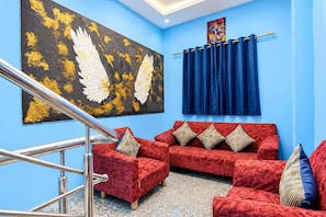 Quarto com sofá vermelho, poltrona vermelha, uma pintura abstrata grande e cortina azul.