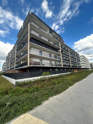 Edifício residencial com várias andares, varandas, um caminho pavimentado e área ajardinada.
