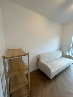 Quarto com mesa de madeira, sofá branco e radiador.