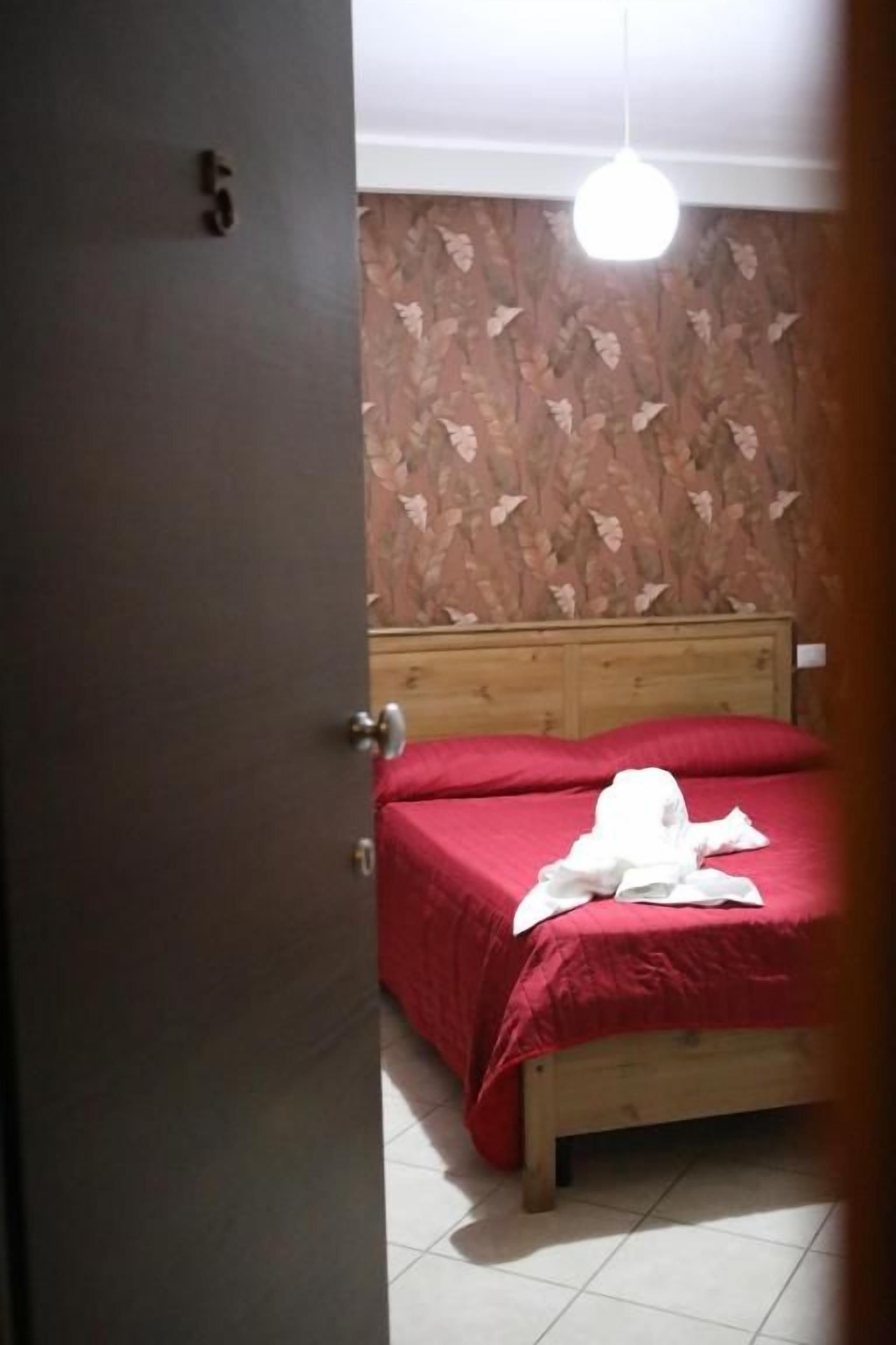 Quarto com cama de madeira, colcha vermelha e parede com padrão de folhas.