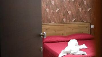 Quarto com cama de madeira, colcha vermelha e parede com padrão de folhas.