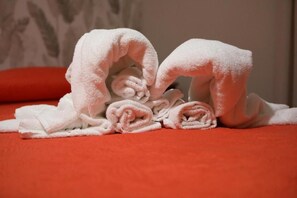 Cama com cobertura vermelha e pilha de toalhas brancas dispostas em formato de coração.