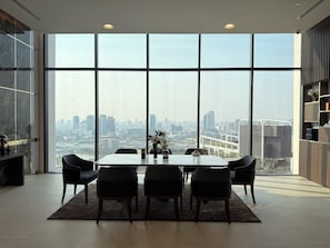 Uma área de refeições moderna com uma mesa grande e cadeiras, janelas amplas com vista para a cidade e decoração minimalista.