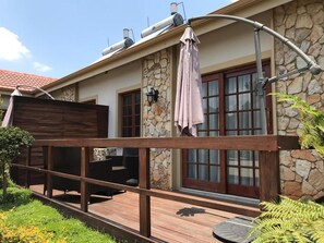 Uma casa com fachada de pedra, um deck de madeira e uma área de pátio com mobiliário de exterior.