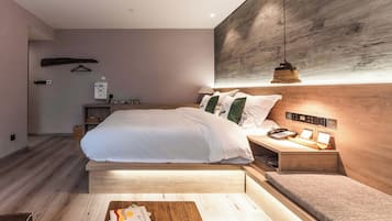 Quarto de hotel moderno com uma cama grande, mesa de cabeceira e painel de madeira.