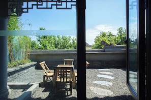 Vista de dentro de um edifício, com um balcão, mesa, cadeiras, grade e vegetação.
