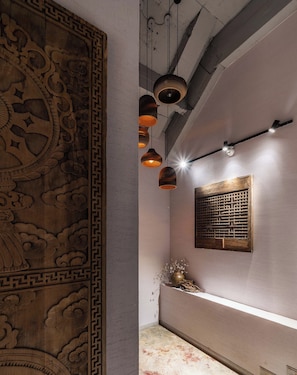 Quarto com painel de madeira decorativo, iluminação pendente, luminária na parede e um pequeno prateleira com objetos decorativos.
