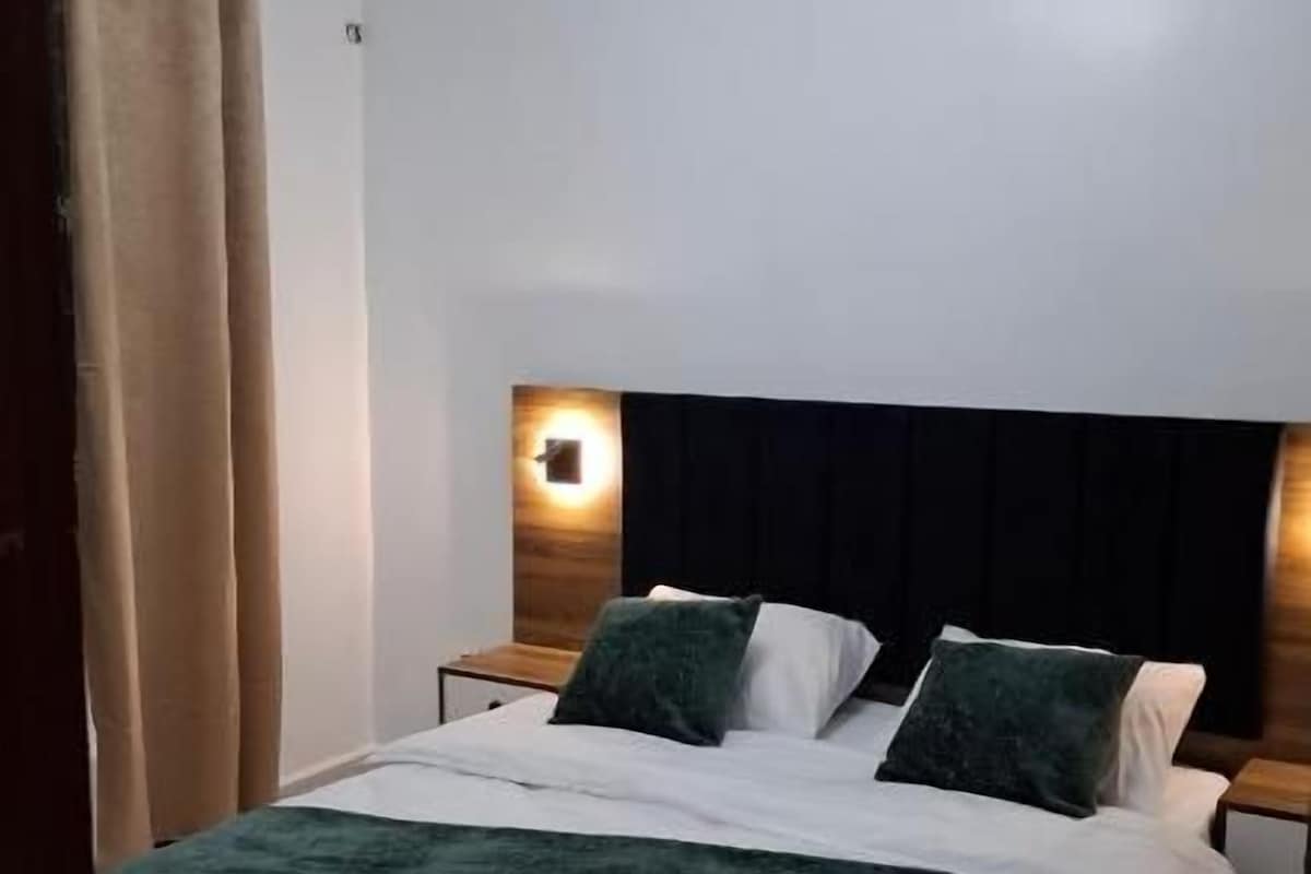 Quarto com cama, mesas de cabeceira, cabeceira e luminária no teto.