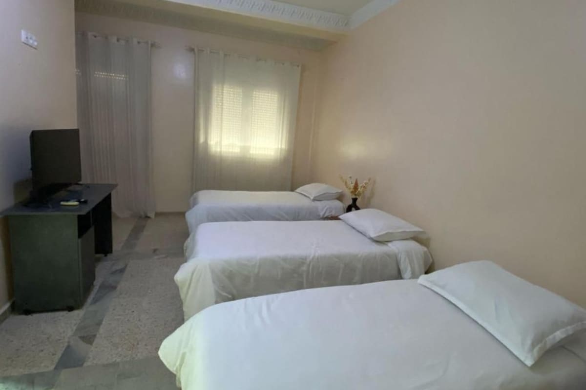 Quarto de hotel com três camas, uma escrivaninha e uma televisão.