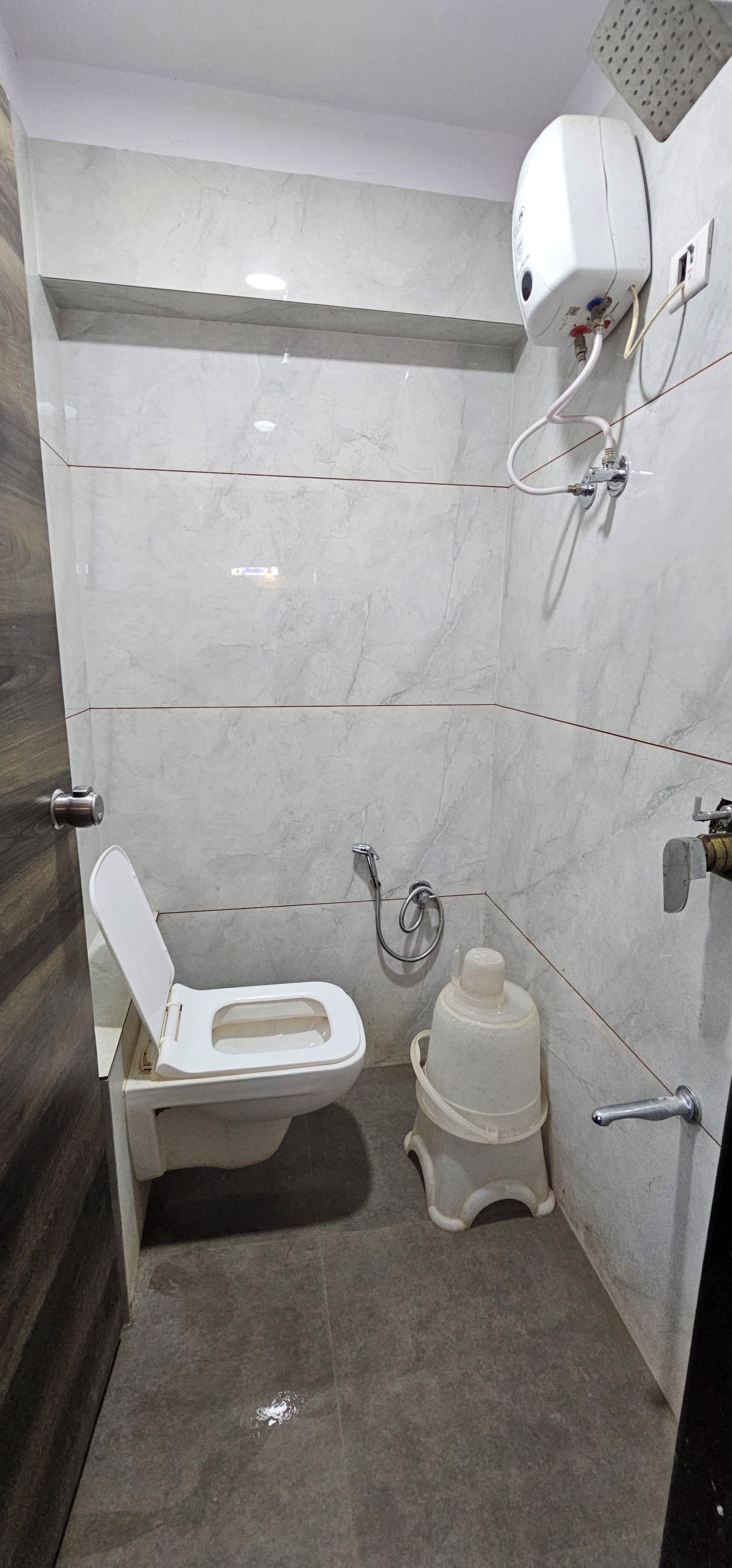 Casa de banho pequena e funcional, com sanita, bidé e chuveiro fixo na parede.